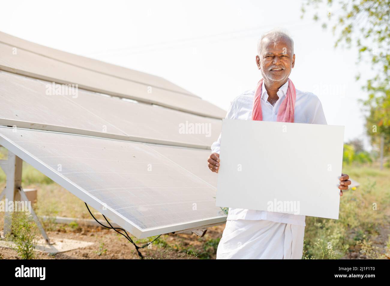 Smiling village farmer showing white empty board by looking at camera ...