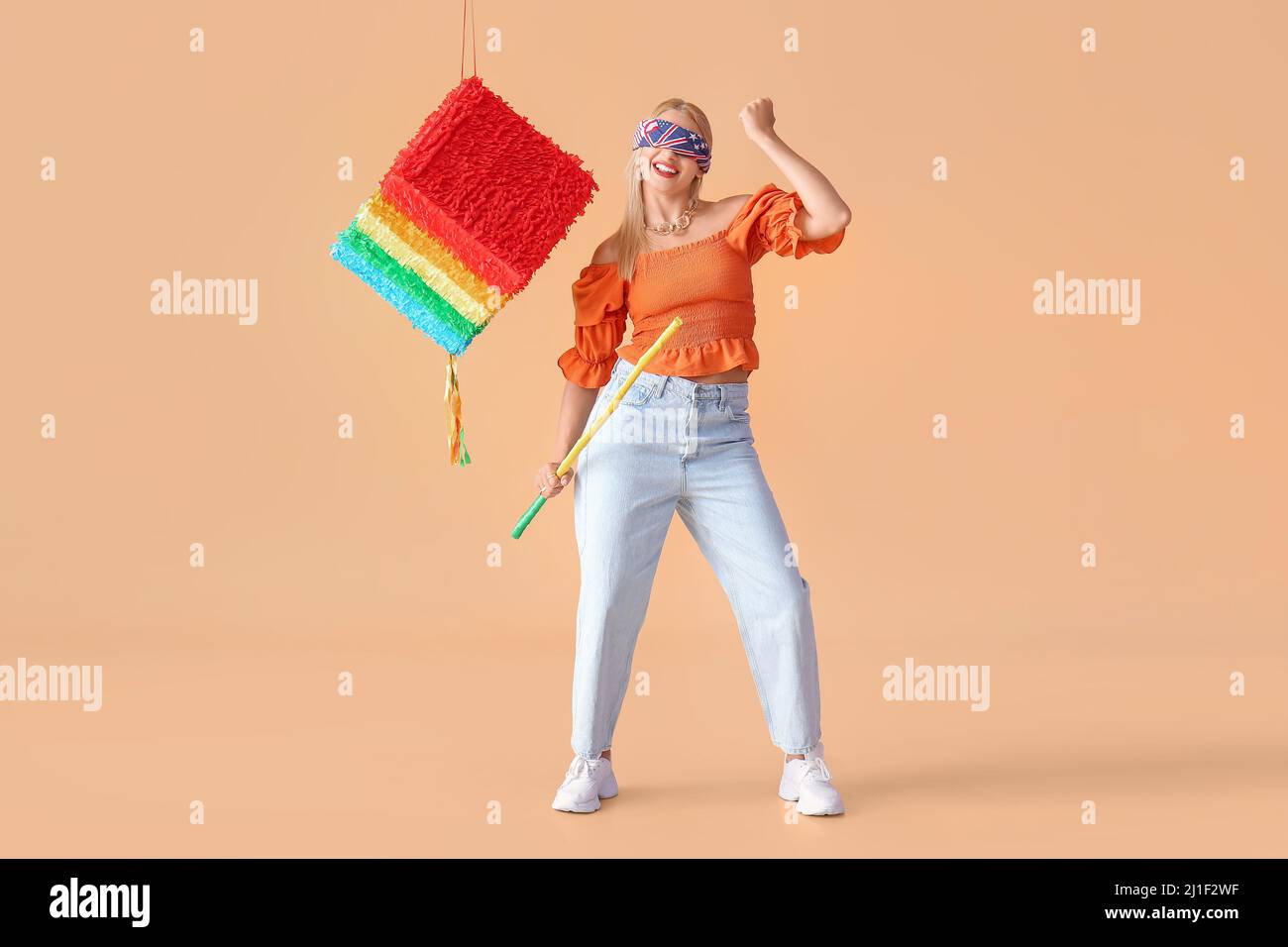 Young woman with blindfold breaking Mexican pinata on beige background ...