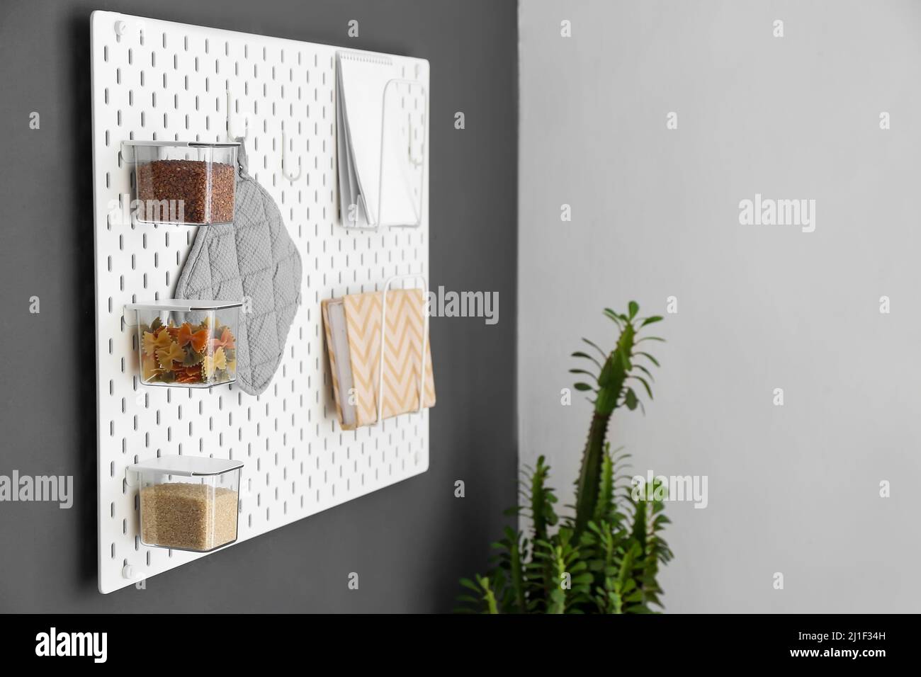 Pegboard with notebooks and jars with food on dark wall in kitchen ...
