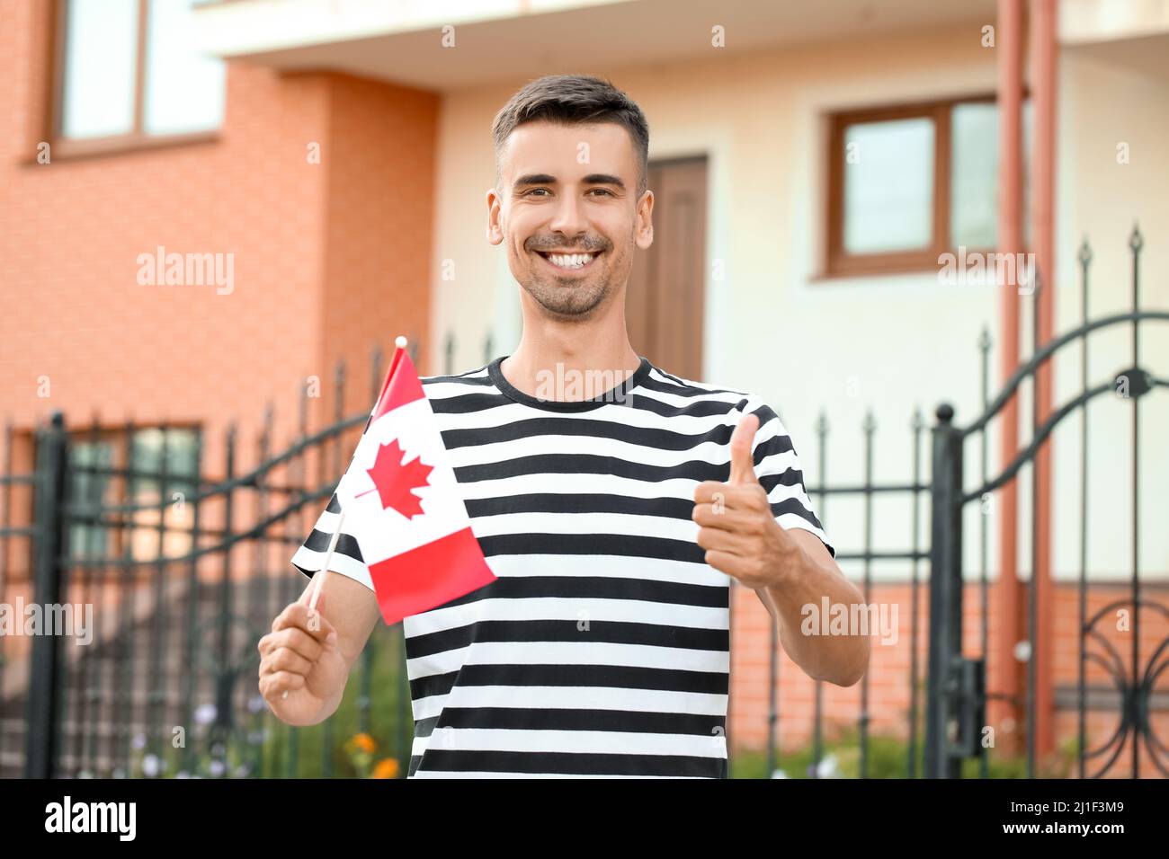 Young man with flag of Canada showing thumb-up outdoors Stock Photo - Alamy