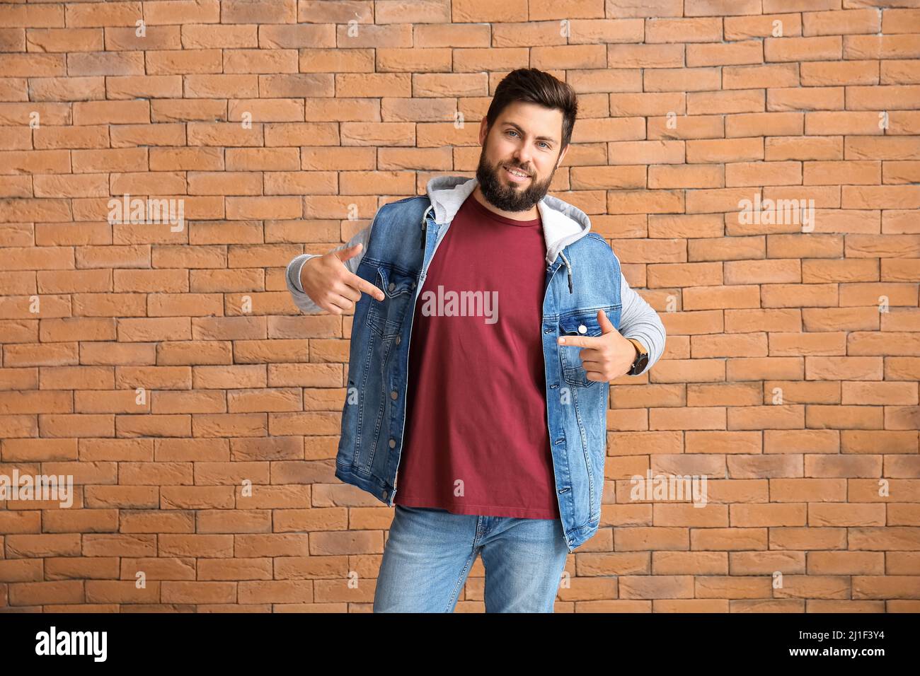 Handsome man pointing at red t-shirt on brick background Stock Photo ...