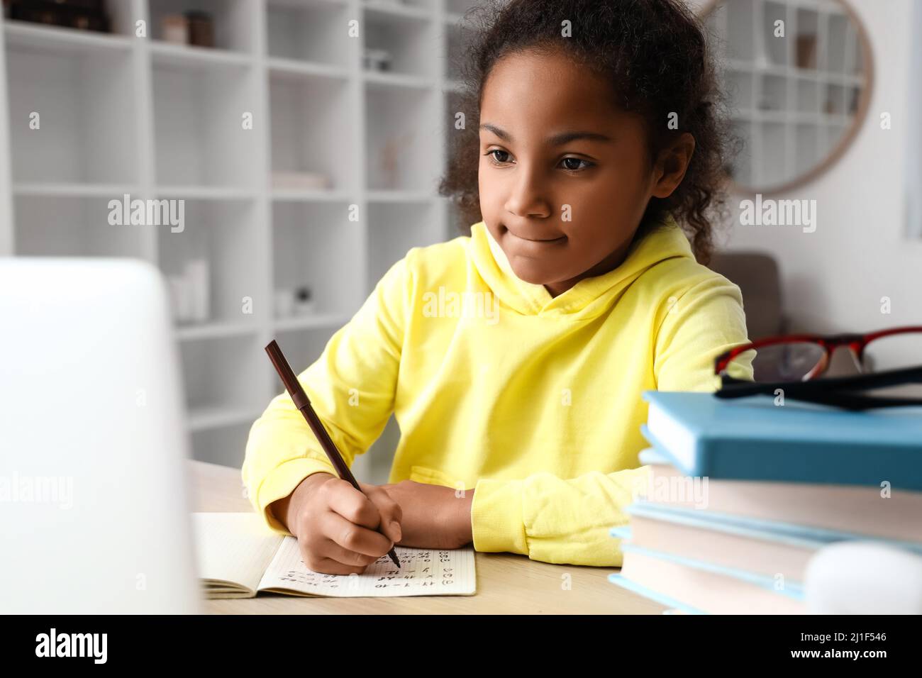 Little African-American girl writing in copybook while studying with ...