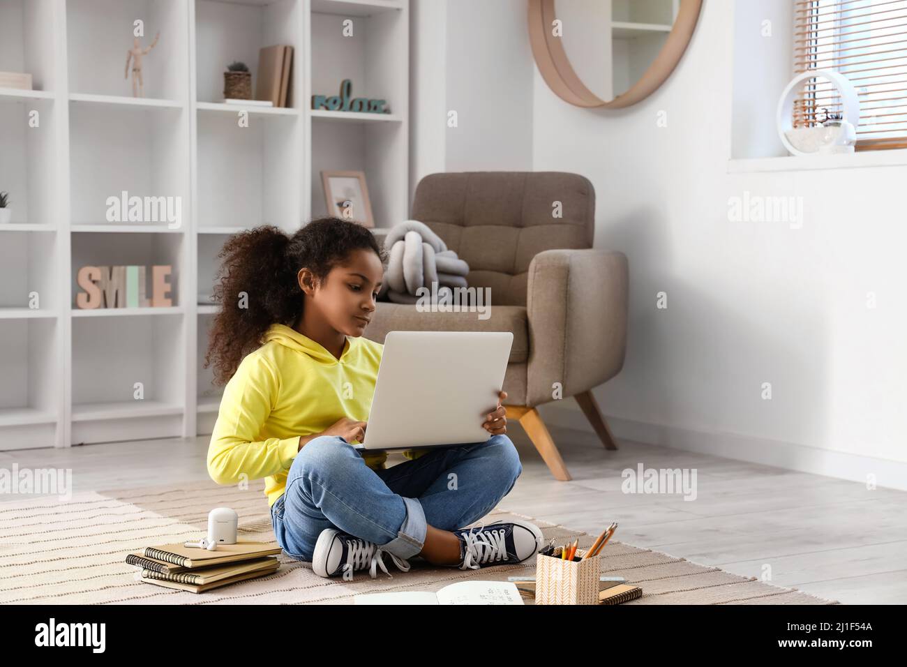 Little African-American girl studying with online tutor on floor at ...