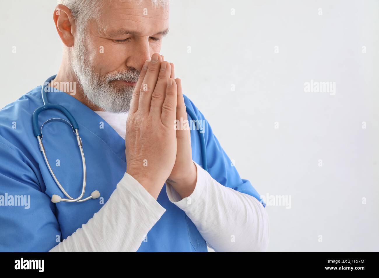 Mature male doctor praying on white background Stock Photo - Alamy