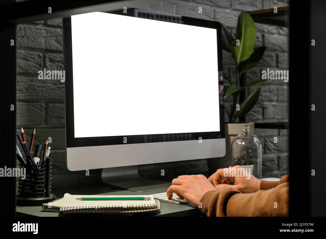 Man working with modern computer in dark room, view through window ...