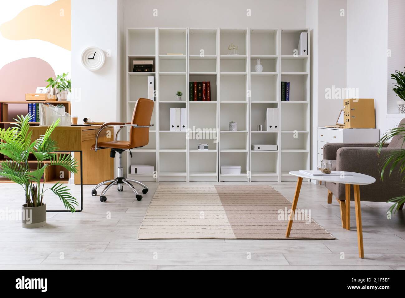 Interior of office with workplace, shelving unit and stylish clock on ...