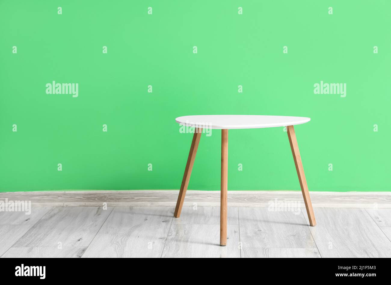 Stylish table near green wall in room Stock Photo - Alamy