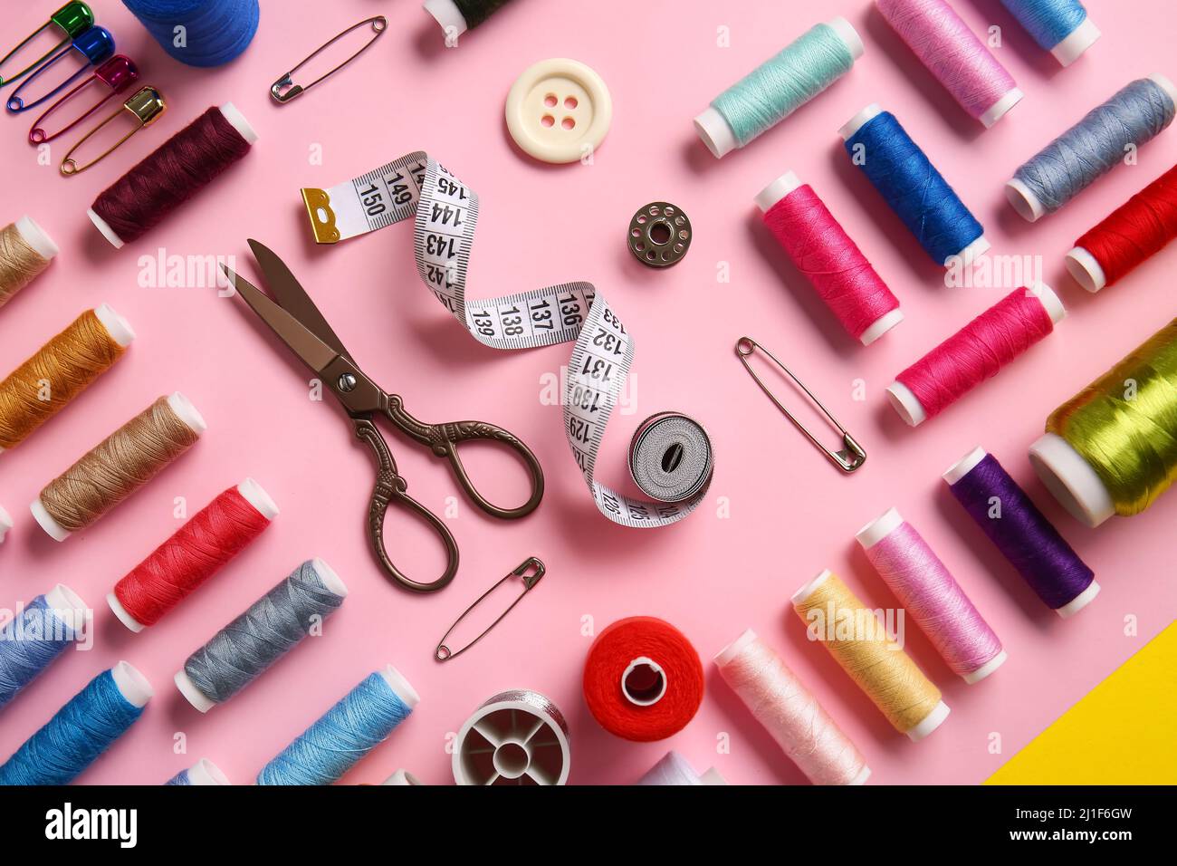 Thread spools, scissors, measuring tape and buttons on pink background ...