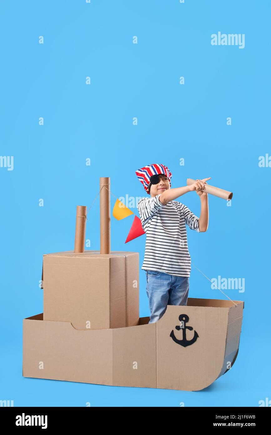 Cute little boy playing with cardboard ship on blue background Stock ...
