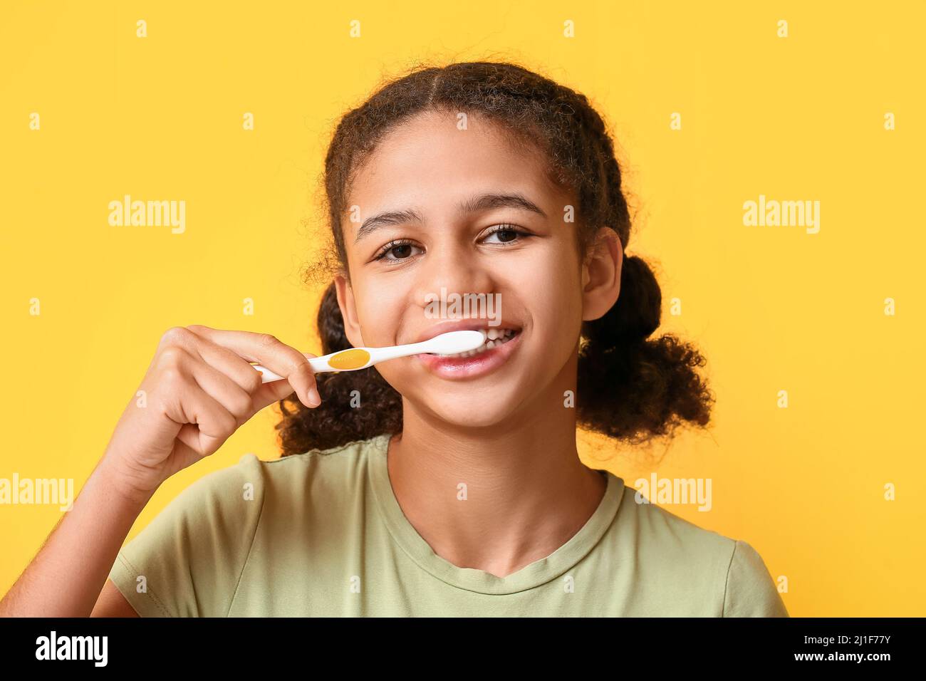 African-American teenage girl brushing teeth on yellow background Stock ...