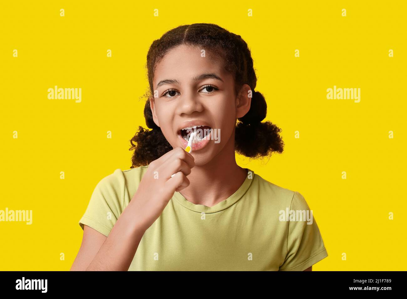 African-American teenage girl brushing teeth on yellow background Stock ...
