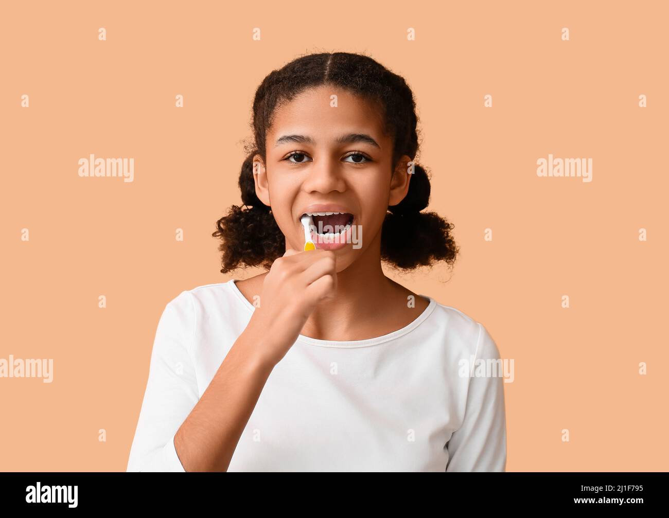 African-American teenage girl brushing teeth on beige background Stock ...