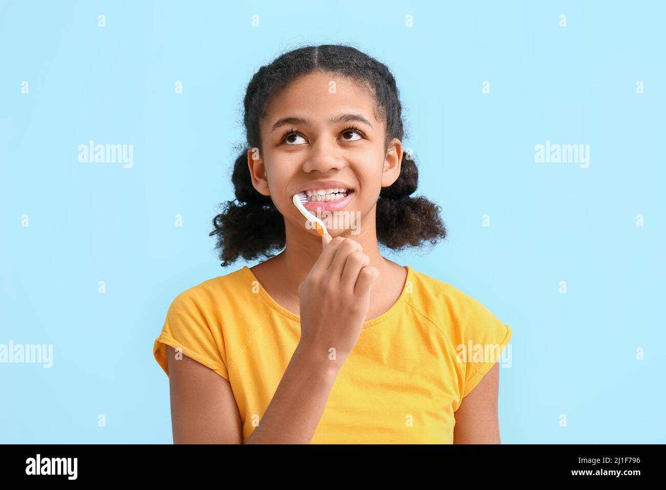 African-American teenage girl brushing teeth on blue background Stock ...