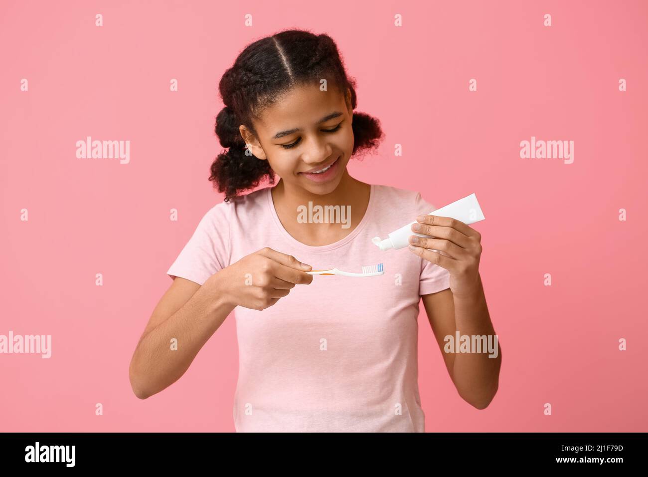 African-American teenage girl applying tooth paste onto brush on pink ...