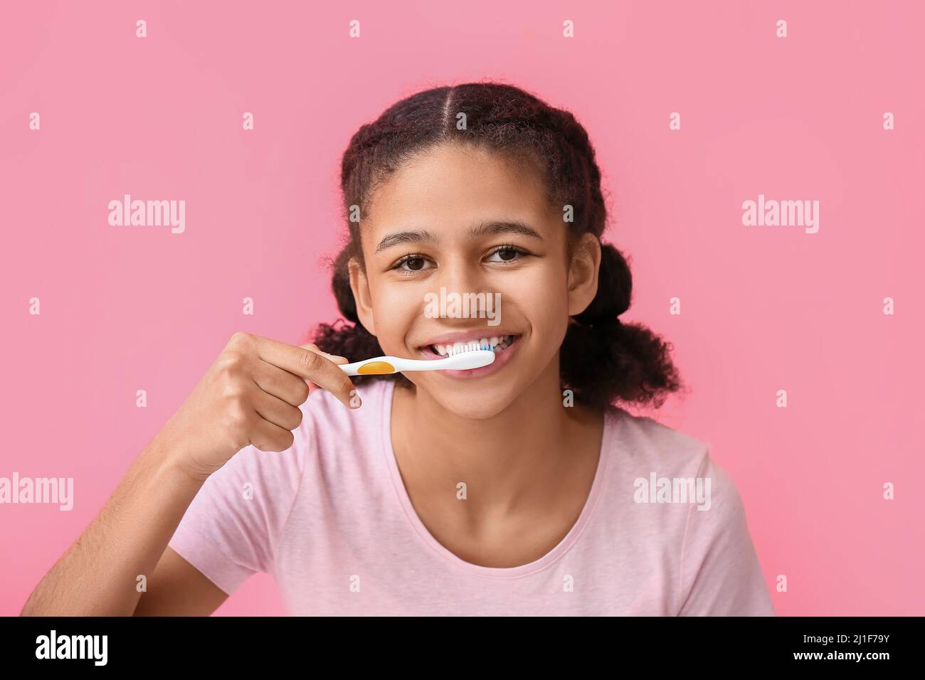 African-American teenage girl brushing teeth on pink background Stock ...