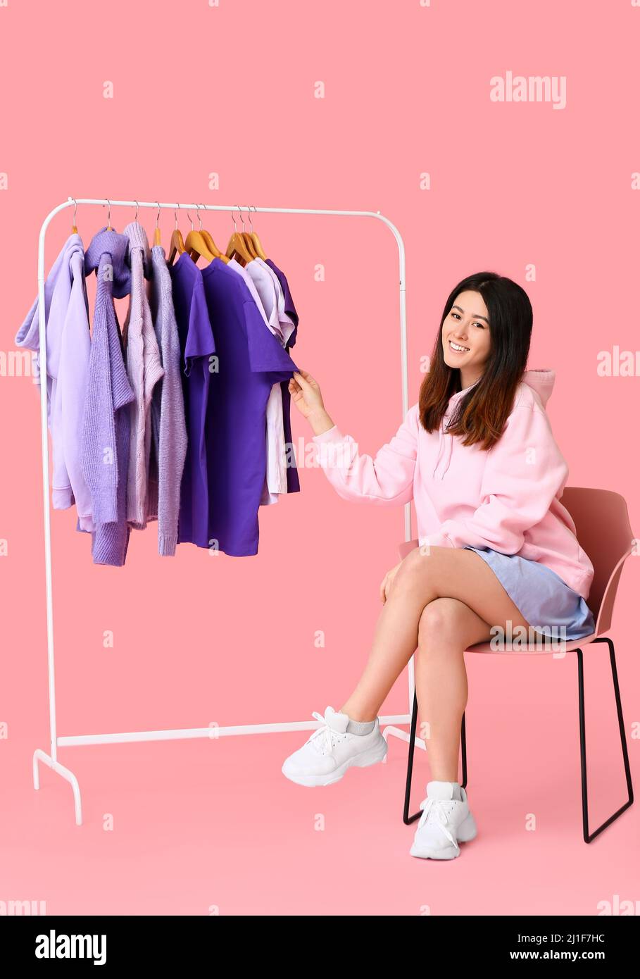 Young Asian woman sitting in chair and rack with clothes on pink ...