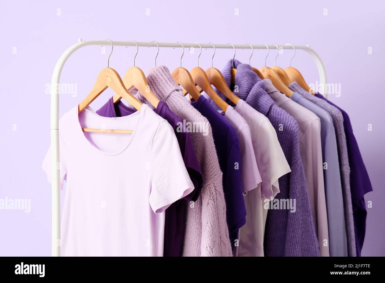 Rack with clothes in purple shades on lilac background Stock Photo - Alamy