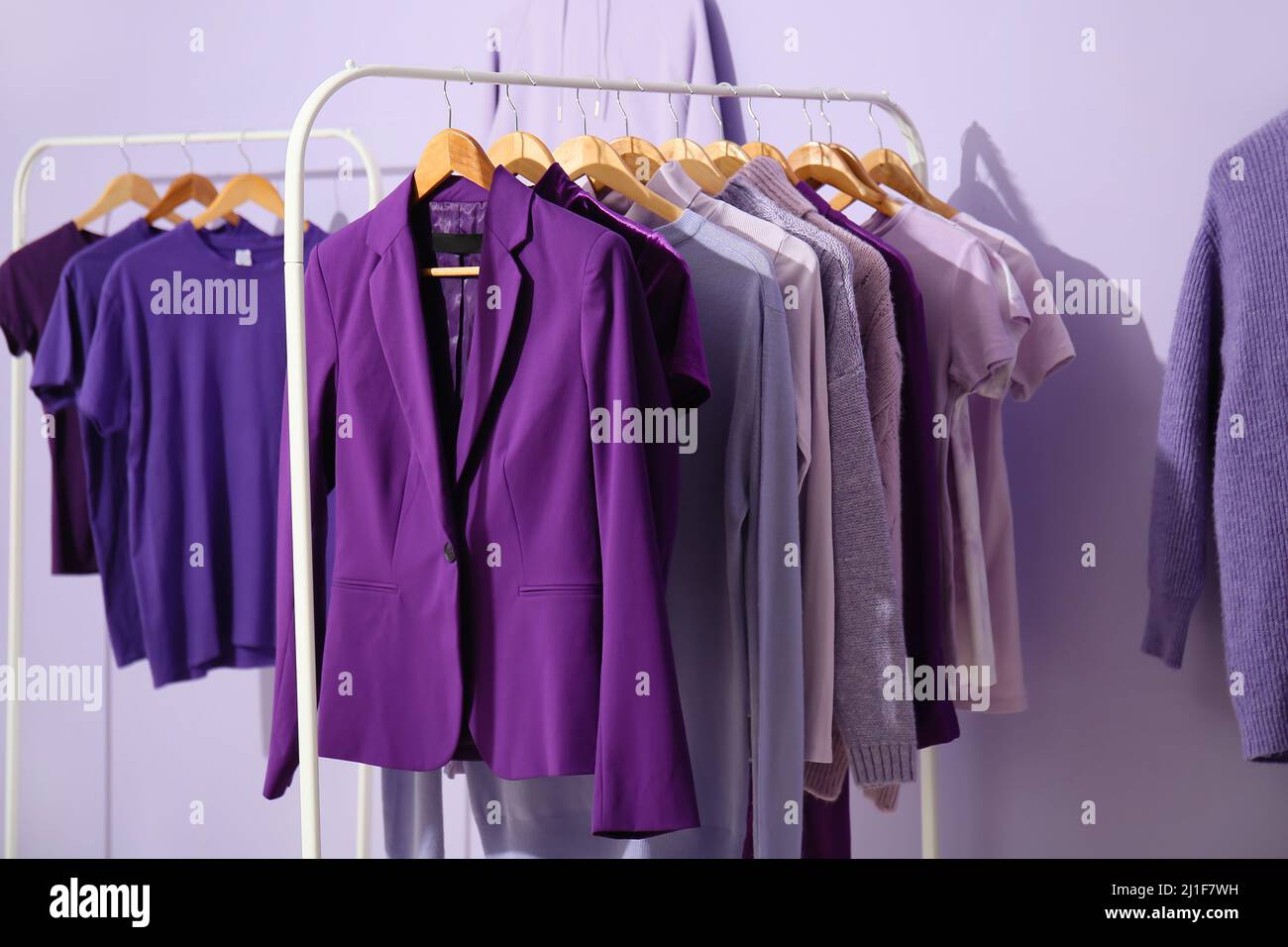 Racks with clothes in purple shades on lilac background Stock Photo - Alamy