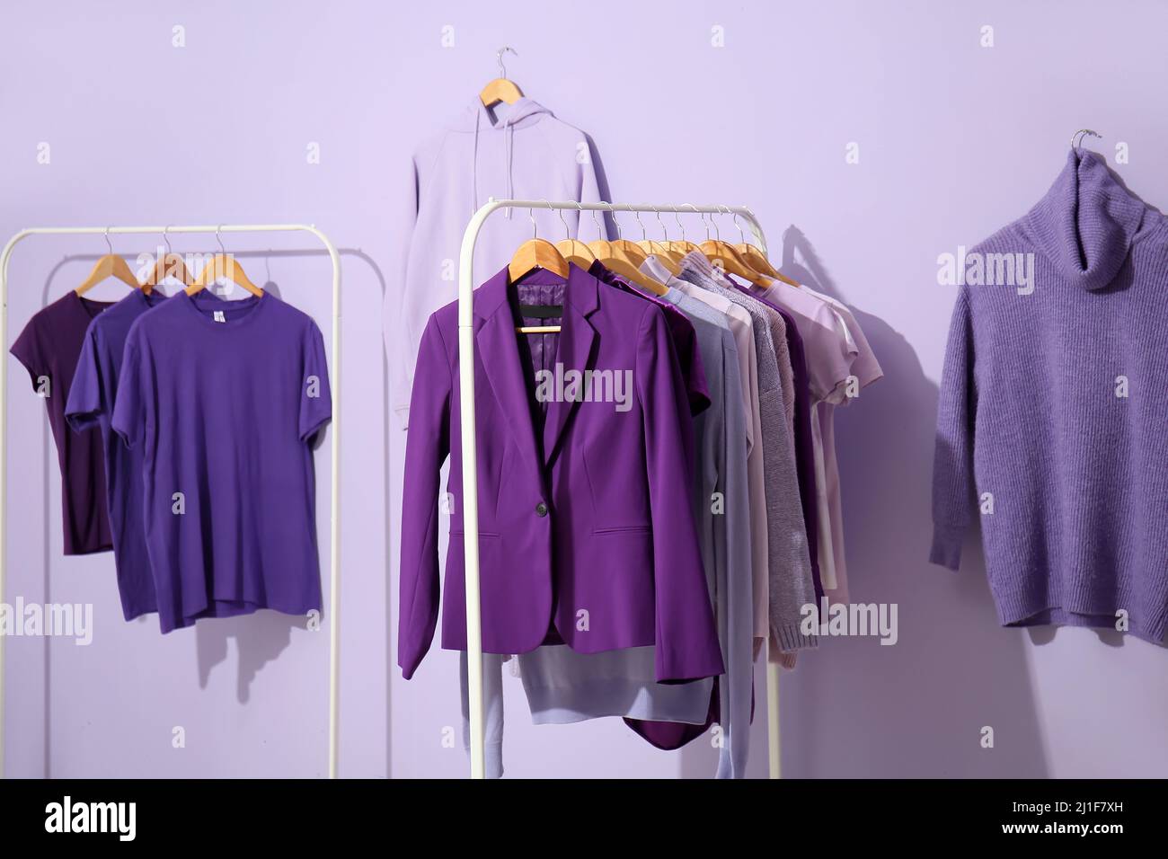 Racks with clothes in purple shades on lilac background Stock Photo - Alamy