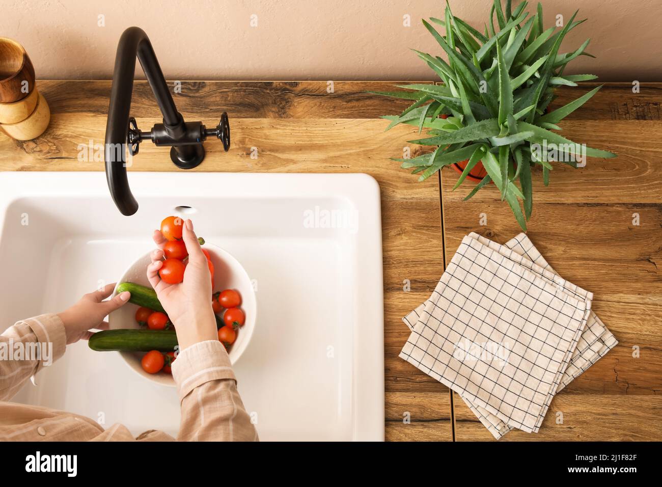 Woman washing fresh vegetables in sink near beige wall Stock Photo - Alamy