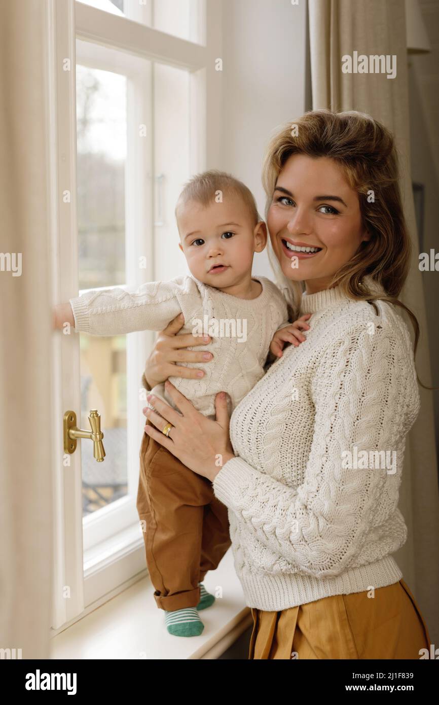 Mother and her little baby son wearing warm sweaters standing by the ...