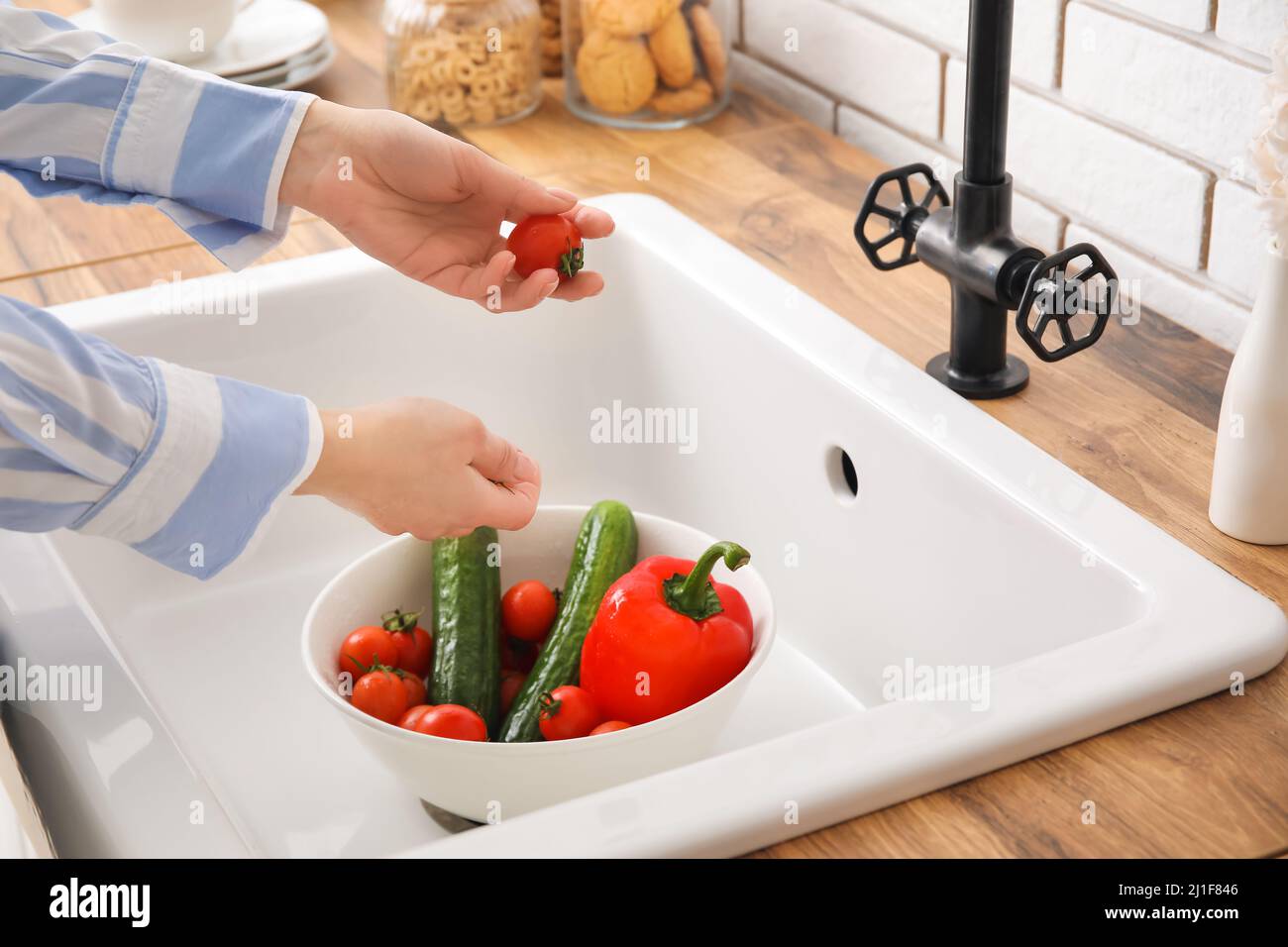 Woman washing fresh vegetables in sink near white brick wall Stock ...