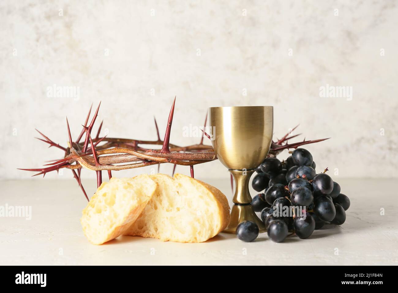 Cup of wine with grapes, bread and crown of thorns on light background ...