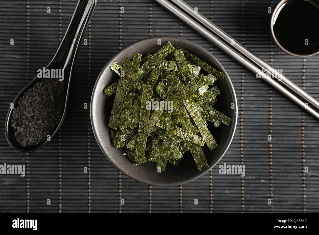 Bowl of chopped seaweed sheets and spoon of sesame on bamboo mat Stock ...