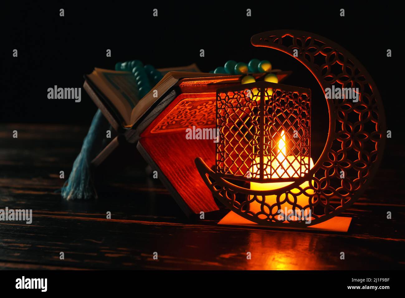 Arabic candle holder with glowing candle, Quran and tasbih on dark ...