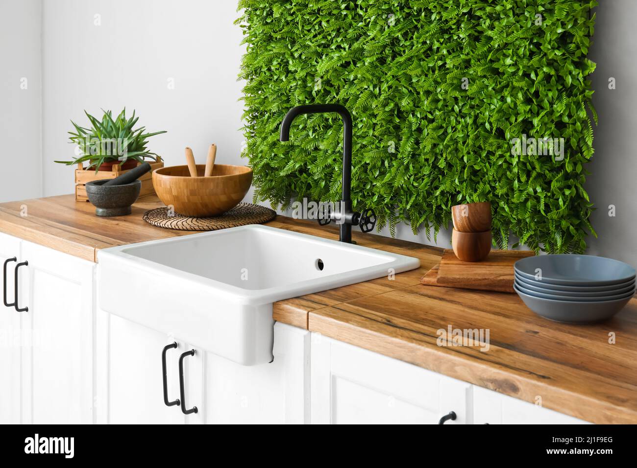 Sink, kitchen utensils and counters near light wall with decorative ...