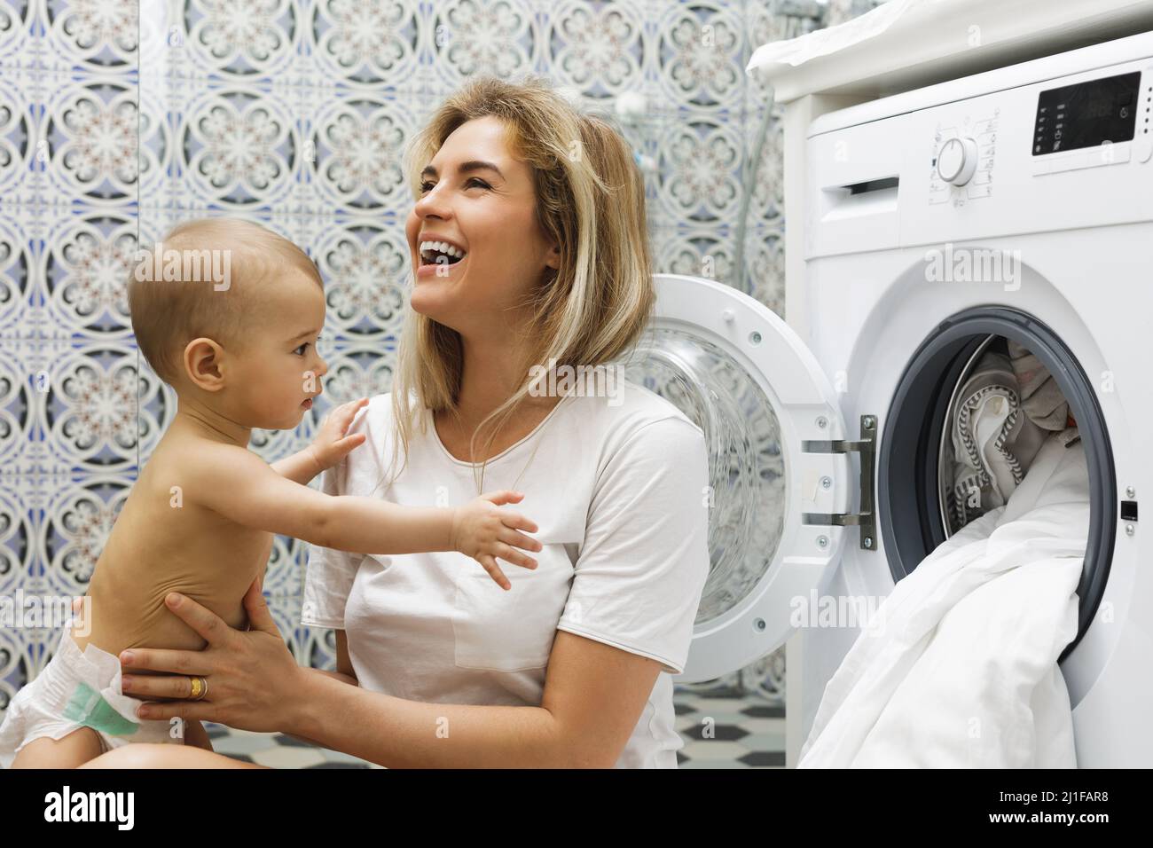 Mother and her little baby son are loading washing machine Stock Photo ...