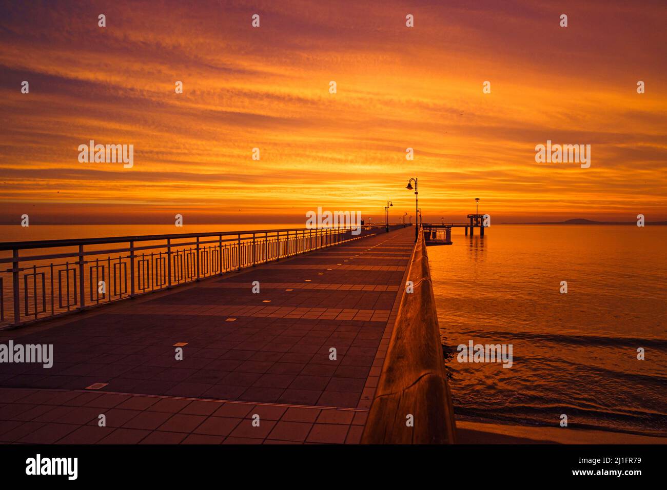 A pier over the ocean during a bright scenic sunset Stock Photo - Alamy