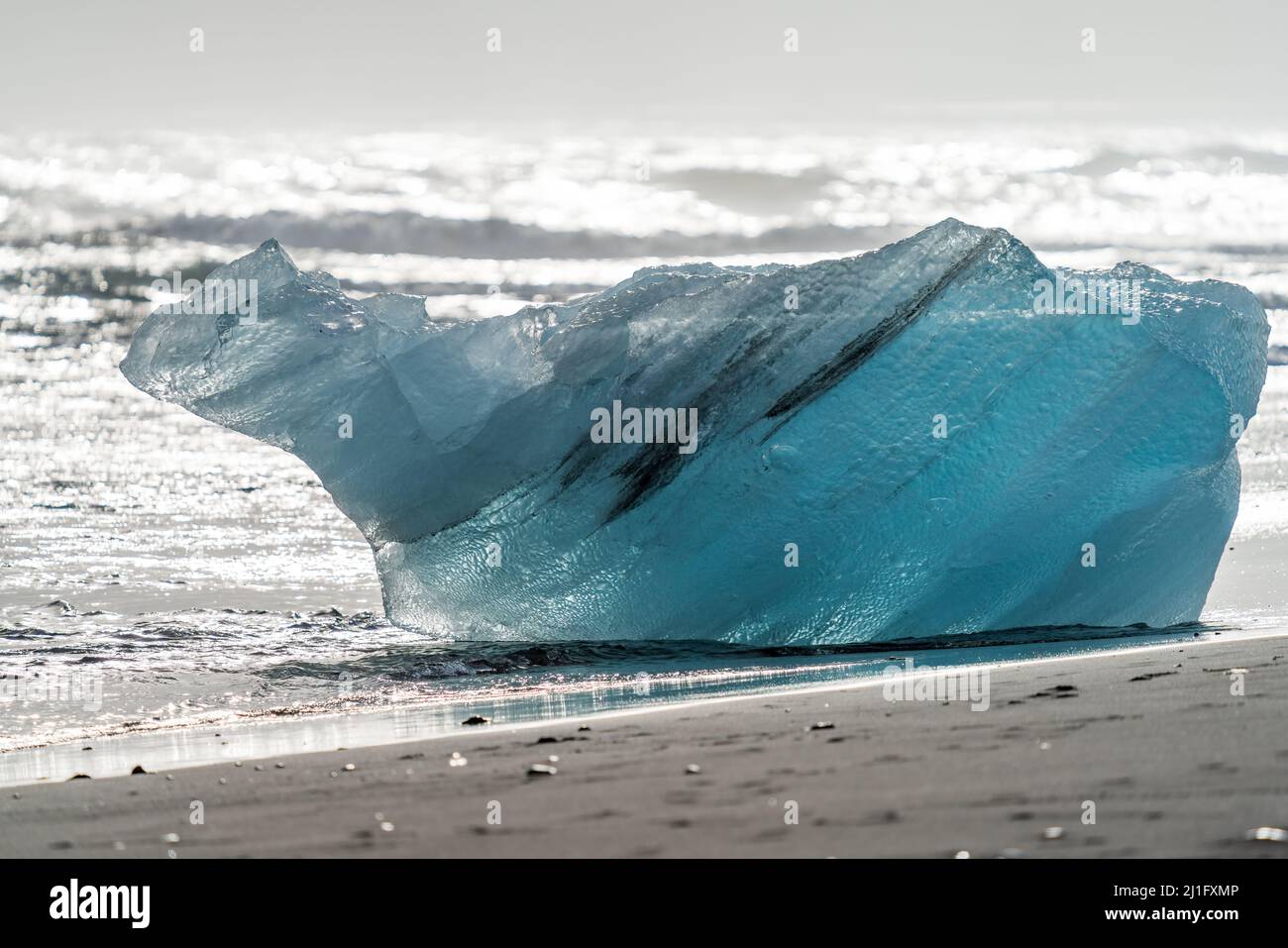 Iceberg backlit over the black sand of diamonds beach in Jokulsarlon ...