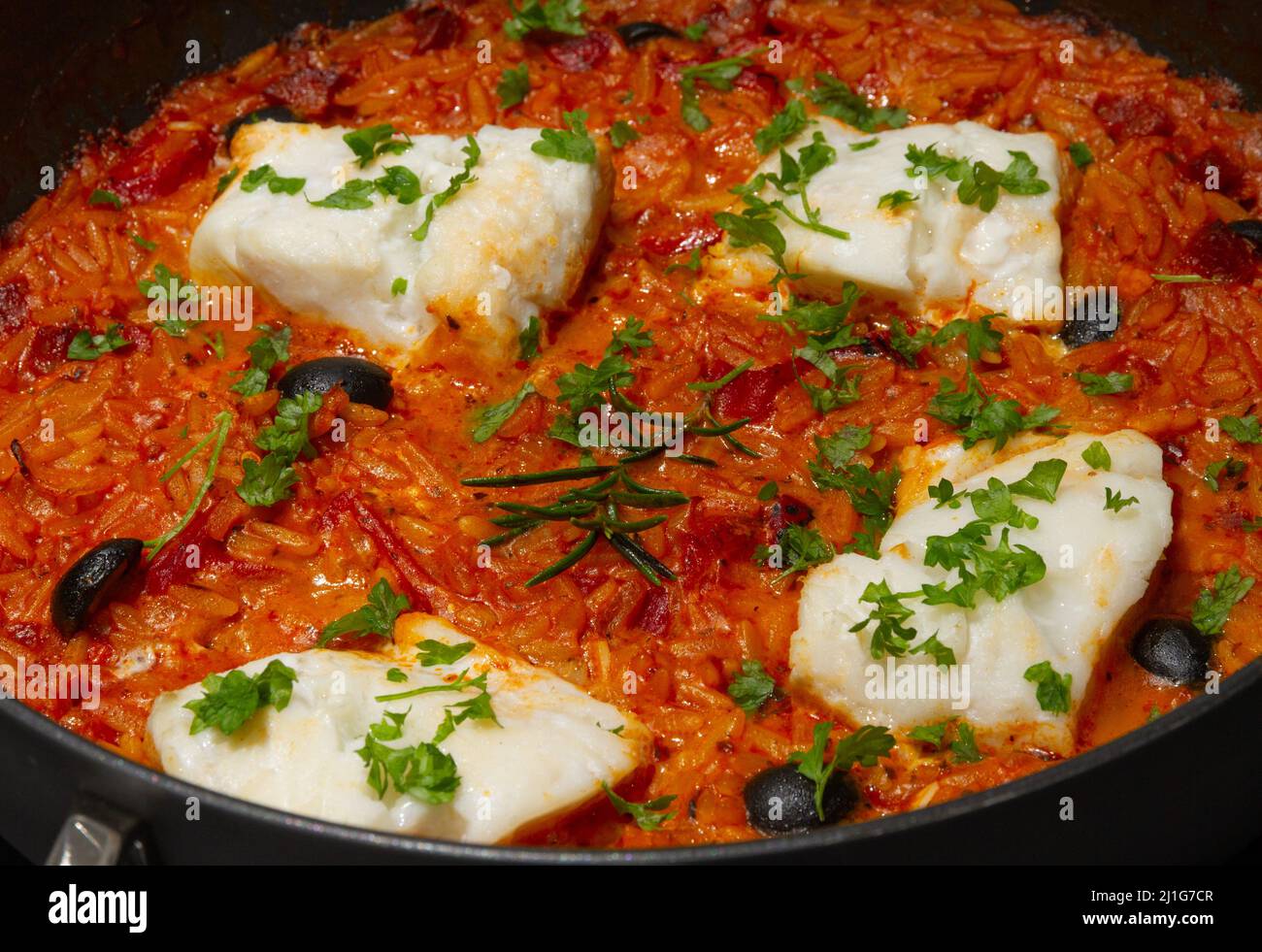 Baked cod with orzo and spicy sausage garnished with chopped parsley ...