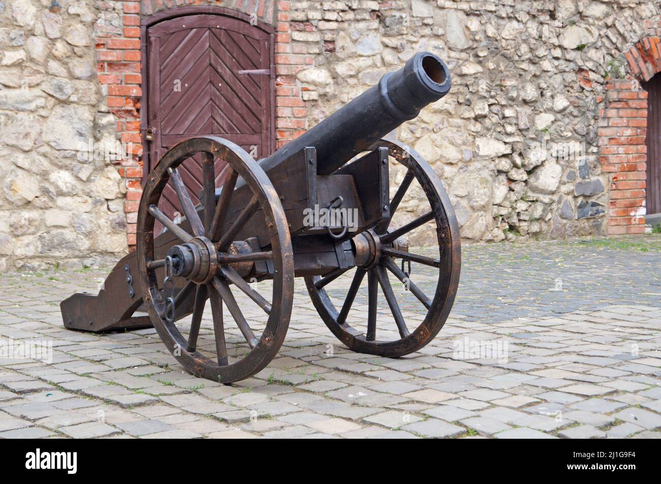 Old iron cannon on wheels near a high castle stone wall on a sunny day ...