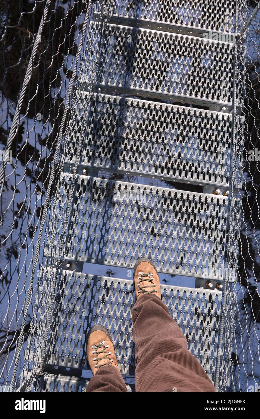 legs of man that walks on the very long suspension bridge in stainless ...