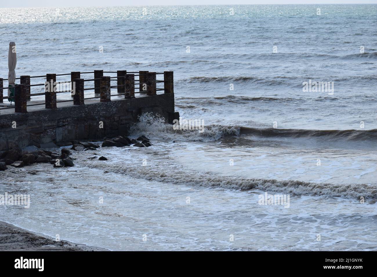 big sea waves splashing against a pier. The pier cuts the sea waves off ...