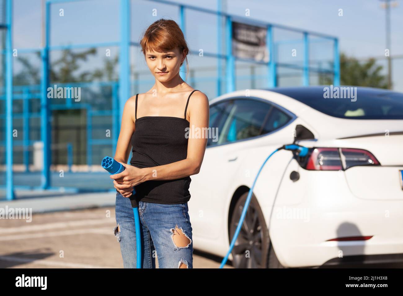 Beautiful young girl next to an electric car. Posing and holding a ...