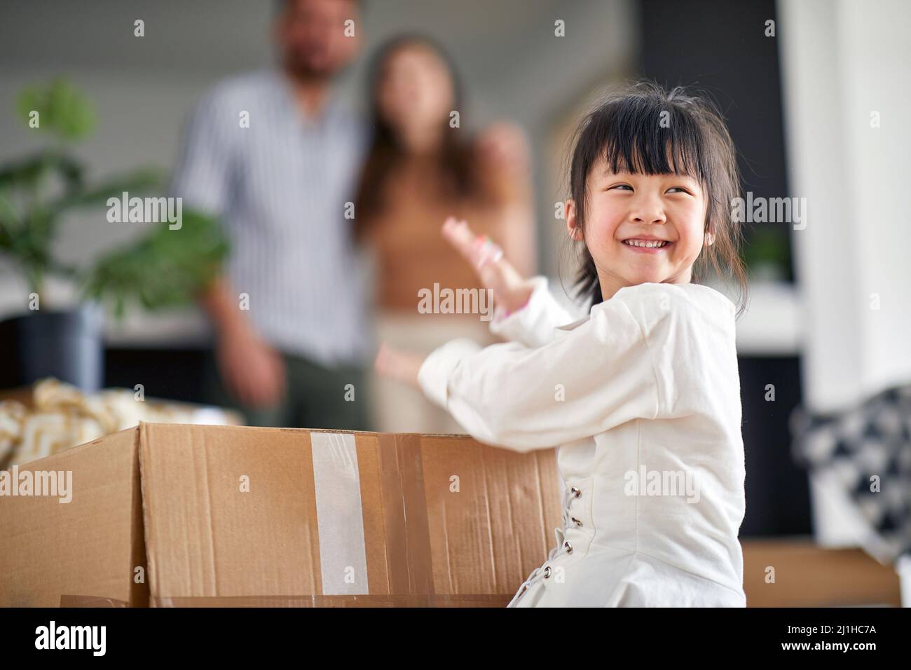 cute little asian girl tapping on cardboard box, smiling, playing with ...