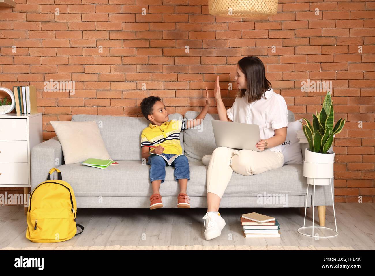 Cute little African-American boy giving high-five to his tutor at home ...