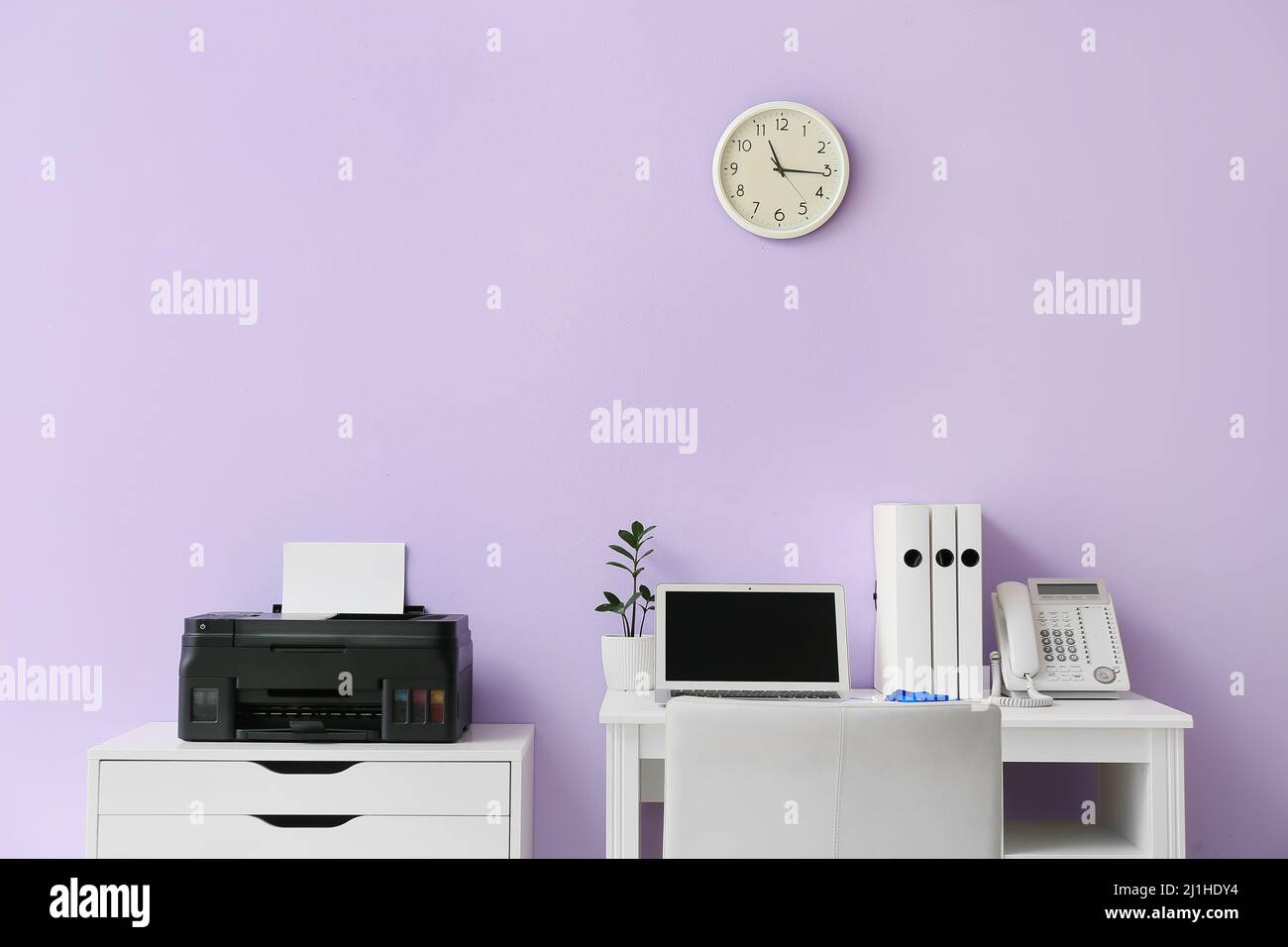 Workplace with modern laptop, chest of drawers with printer and clock ...