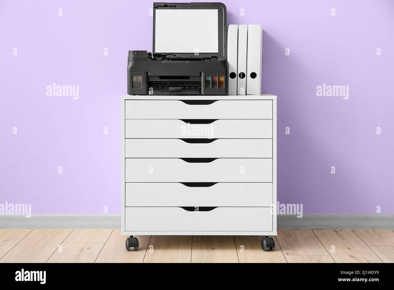 Modern copy machine and folders on chest of drawers near color wall ...