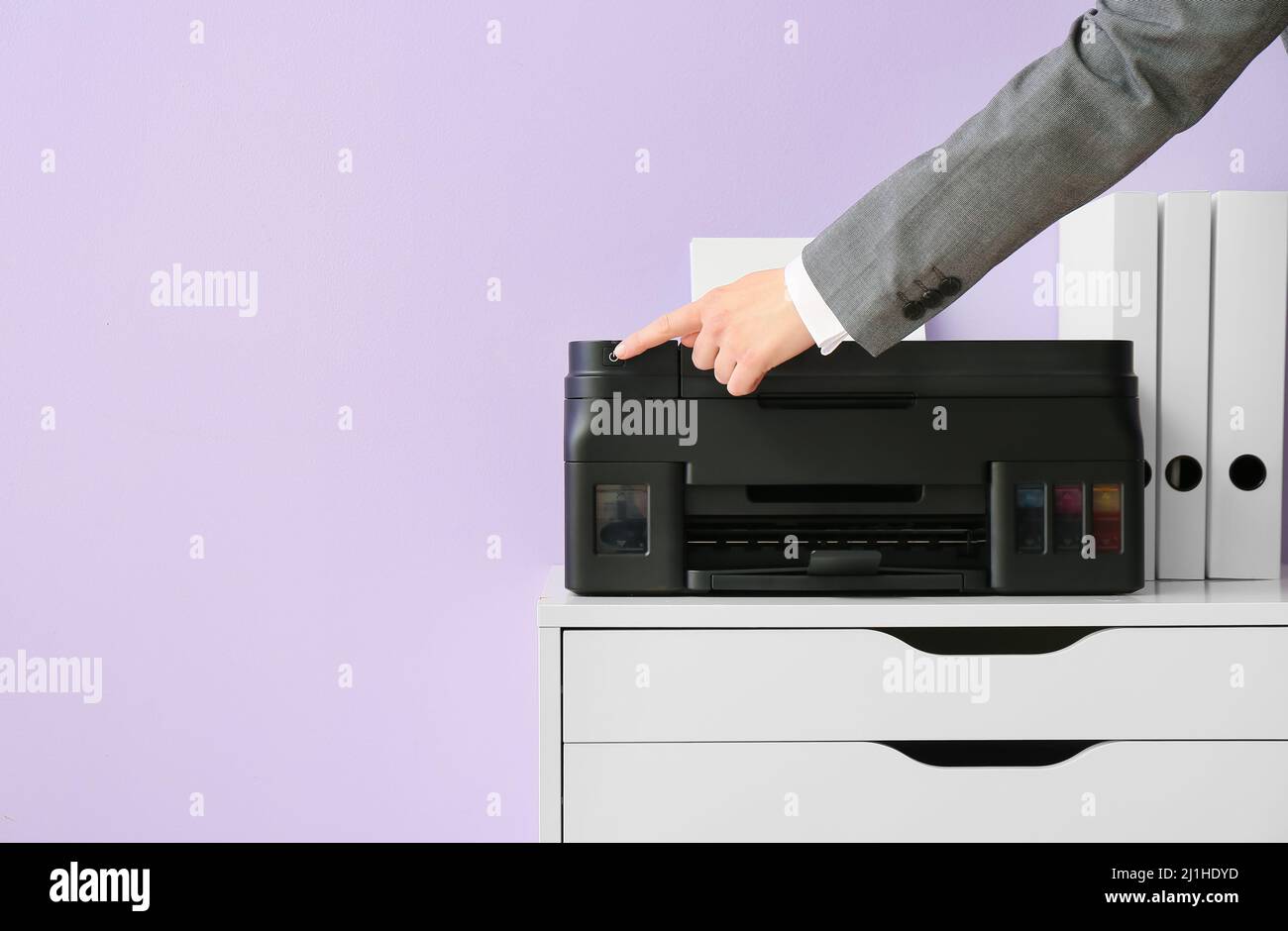Businesswoman using modern printer on chest of drawers near color wall ...