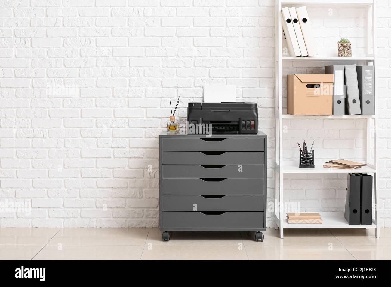 Chest of drawers with modern printer and shelf unit near white brick ...