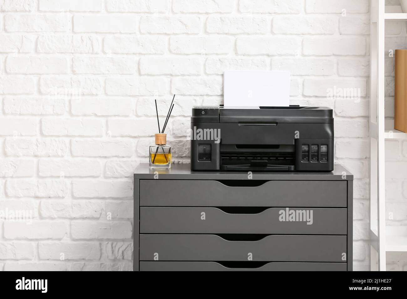 Chest of drawers with modern printer and reed diffuser near white brick ...