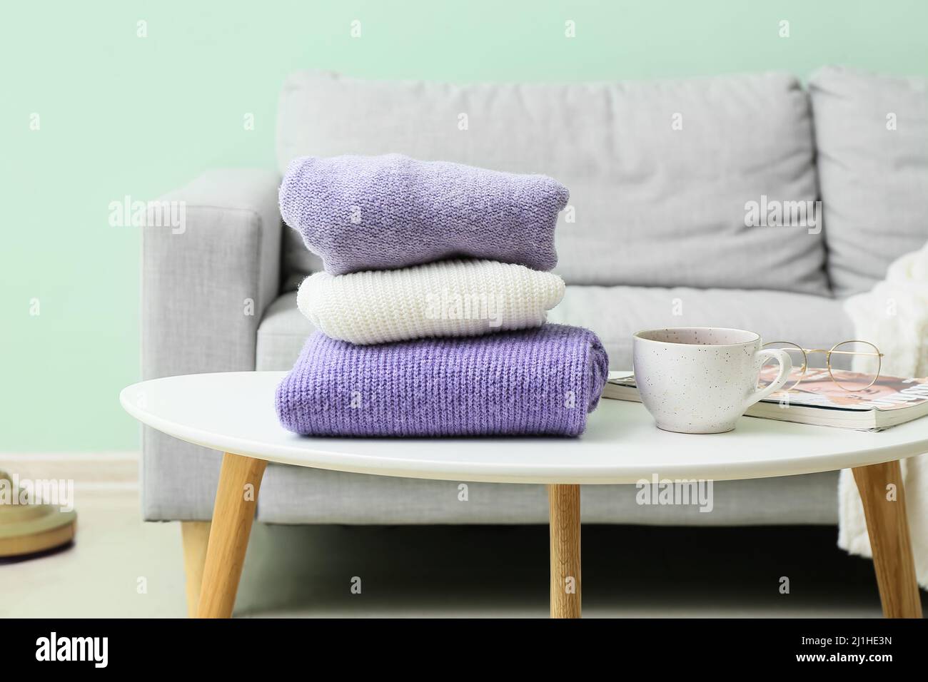 Stack of knitted sweaters and cup on table in room Stock Photo - Alamy