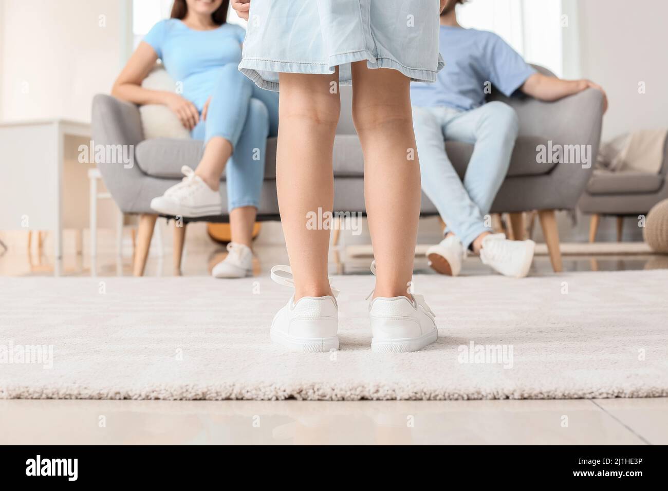 Little daughter standing opposite her parents sitting on sofa Stock ...