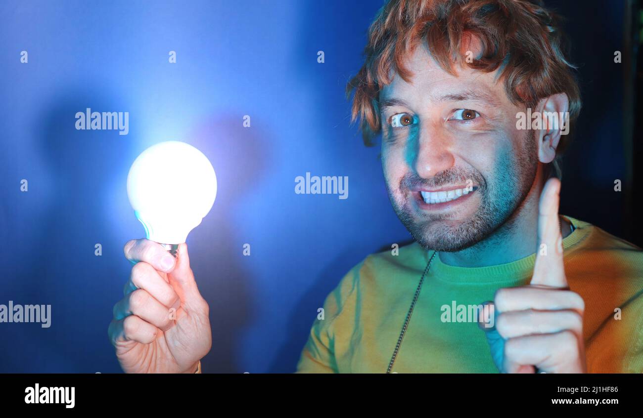 Happy Guy Showing Energy-Saving Lightbulb Standing Over Blue Studio ...