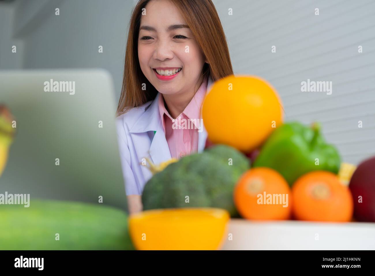Portrait of Asian smiling female nutritionist typing on laptop computer ...