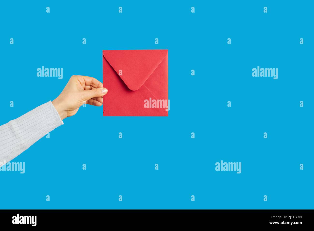 Hand holding red envelope with letter, message or notice against blue ...